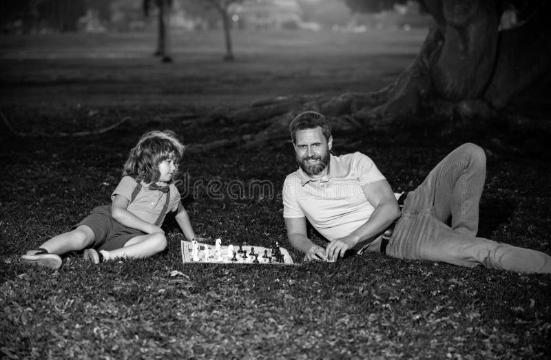 Son Laying on Grass and Playing Chess with Father. Young Boy Beating a ...