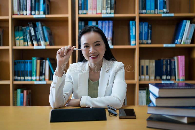 Southeast Asian Female Lecturer Sits at a Small Table, Working at the ...