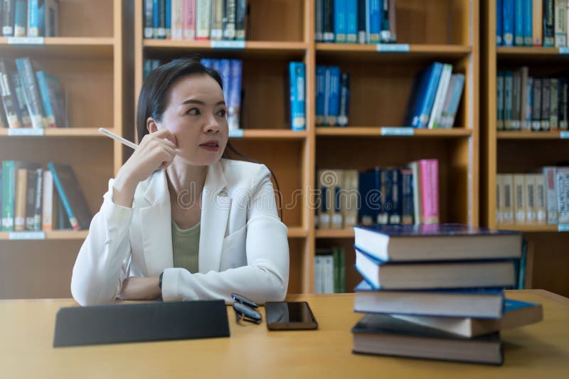 Southeast Asian Female Lecturer Sits at a Small Table, Working at the ...