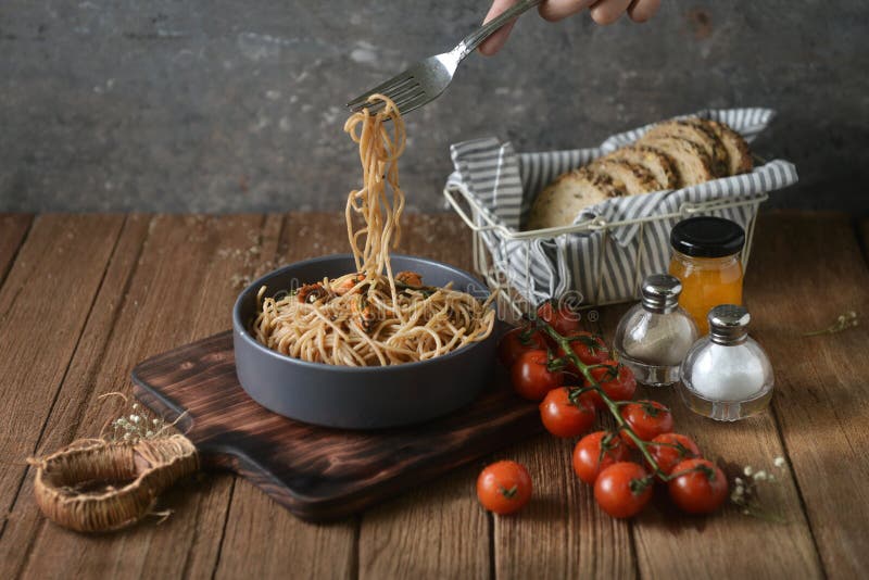 Spaghetti is Pulled Up by the Fork in Hand from Dish and Wooden Plate ...