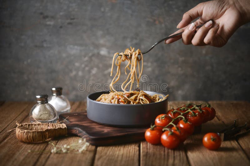 Spaghetti is Pulled Up by the Fork in Hand from Dish and Wooden Plate ...