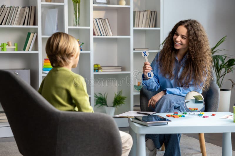 Long-haired Young Speech Therapist Working with a Blonde Boy and Both ...