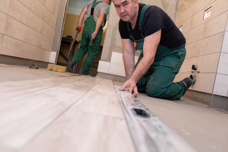 A Builder Checks the Surface Level of Tiles Laid on the Bathroom Floor ...