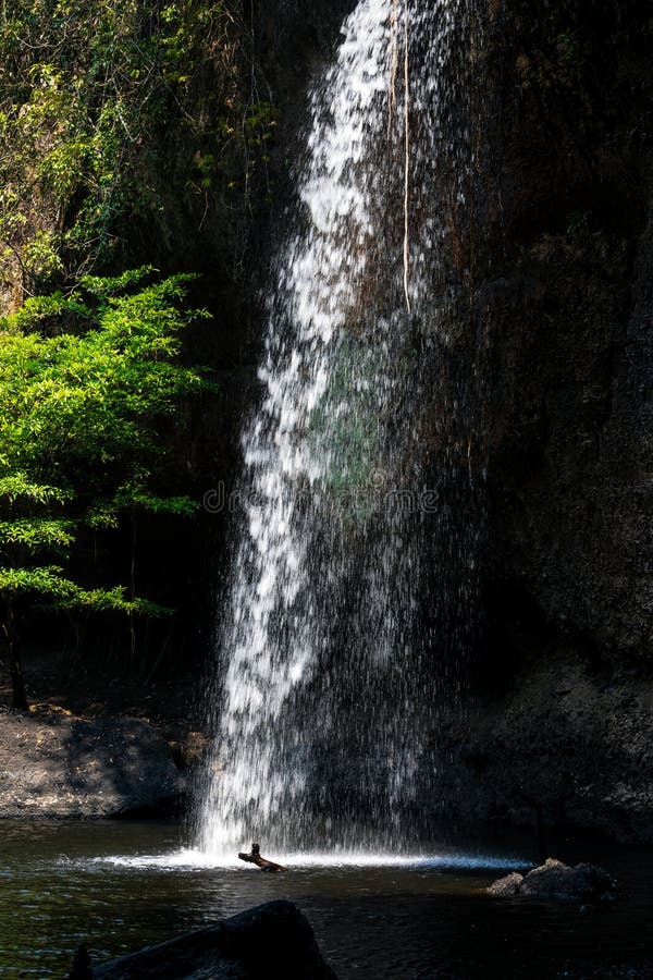Splashing Waterfall with Bright Sunlight Drop on Pond with Dark Cave ...