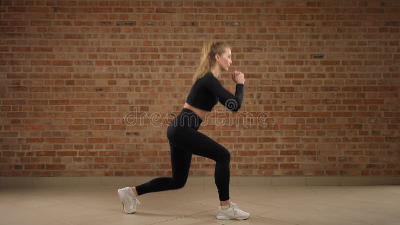 Fitness Trainer Demonstrates Split Squat in Empty Hall with Brick Wall ...