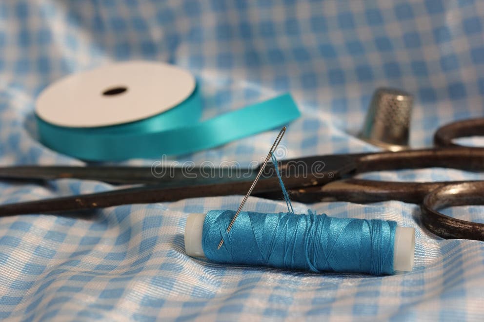 Spool of Blue Thread, Thimble and Needle on Blue and White Fabric Stock ...