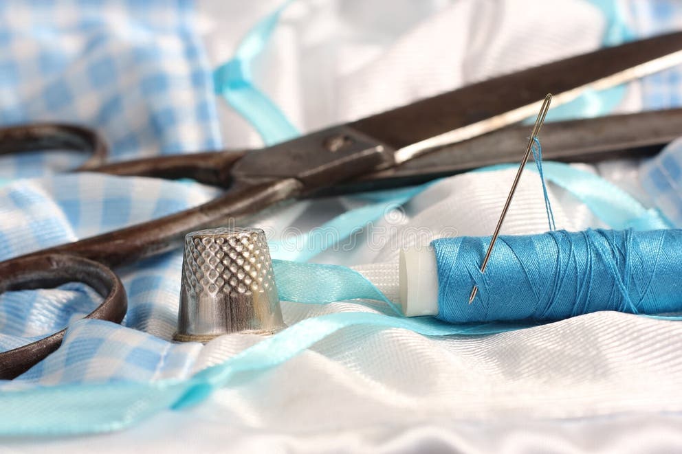 Spool of Blue Thread, Thimble and Needle on Blue and White Fabric Stock ...