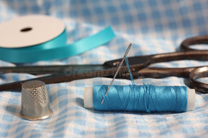 Spool of Blue Thread, Thimble and Needle on Blue and White Fabric Stock ...