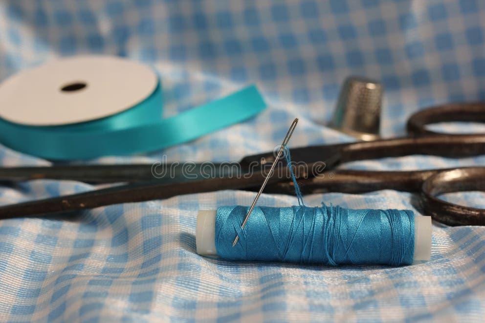 Spool of Blue Thread, Thimble and Needle on Blue and White Fabric Stock ...