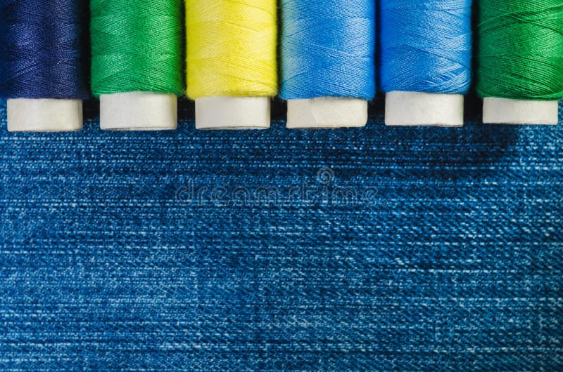 Spools of Green, Yellow and Blue Threads Arranged in Row on Denim with ...