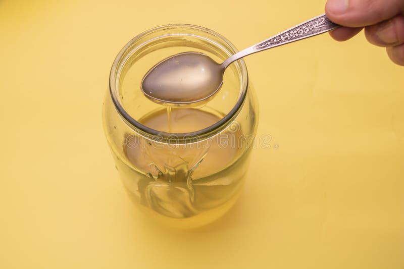 A Spoon with Honey and Liquid in it is Being Held Over a Jar of Clear ...