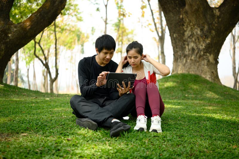 Sporty Couple Sitting on the Grass in a Peaceful Park and Using Digital ...