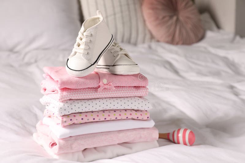 Stack of Baby Girl`s Clothes, Rattle and Shoes on Bed. Space for Text ...