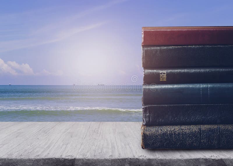 Stack of Book and a Holy Bible on Wooden Table Over Sea and Blue Sky ...