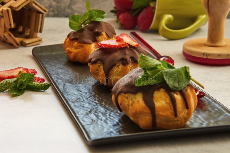 Stack Eclair of Profiteroles with Dark Melted Chocolate on a Black Dish ...
