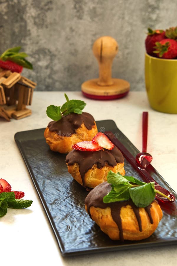 Stack Eclair of Profiteroles with Dark Melted Chocolate on a Black Dish ...