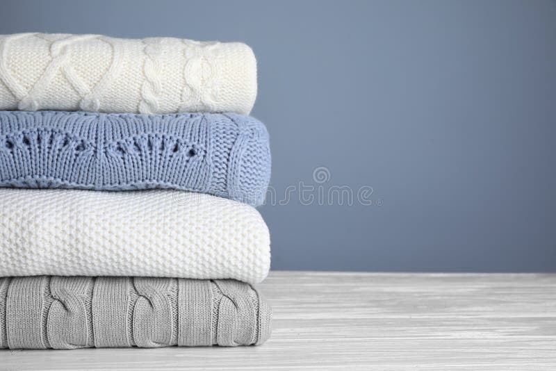Stack of Folded Knitted Sweaters on White Table Against Grey Background ...