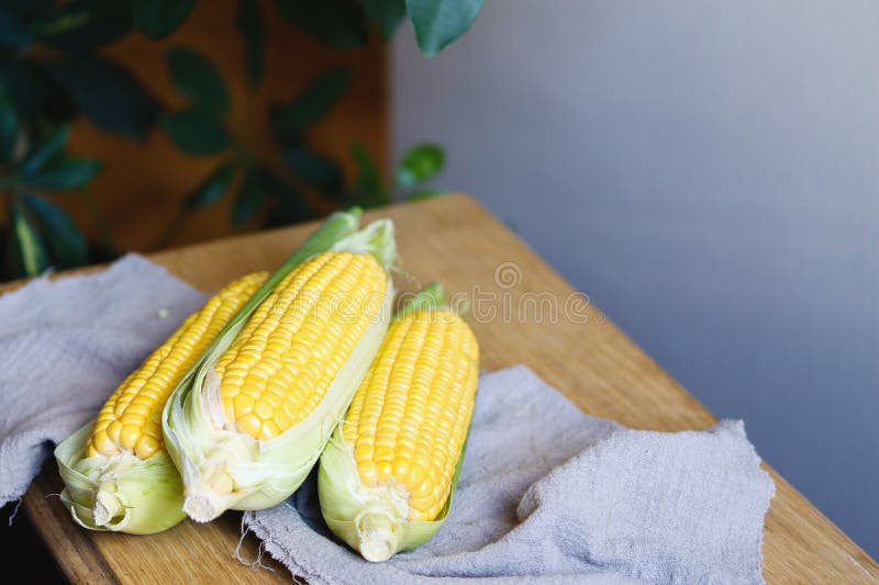 Stack of Fresh Corn Cobs with Leaves on a Wooden Table Over Grey Wall ...