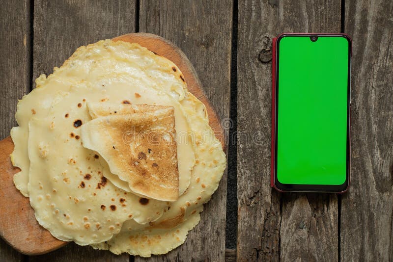 Stack of Fried Pancakes on a Wooden Table and a Phone with a Green ...