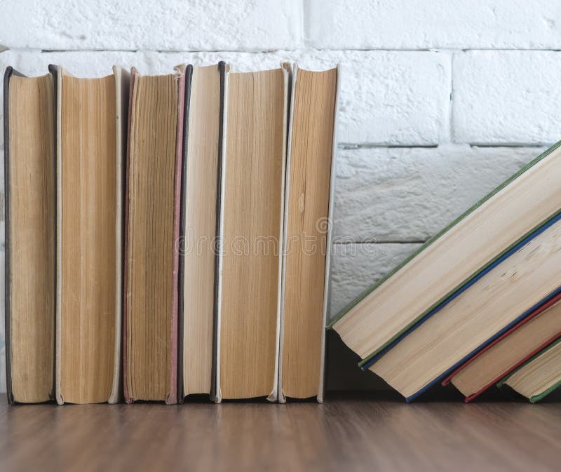A Stack of Hardcover Books on a Wooden Table Against a White Brick Wall ...