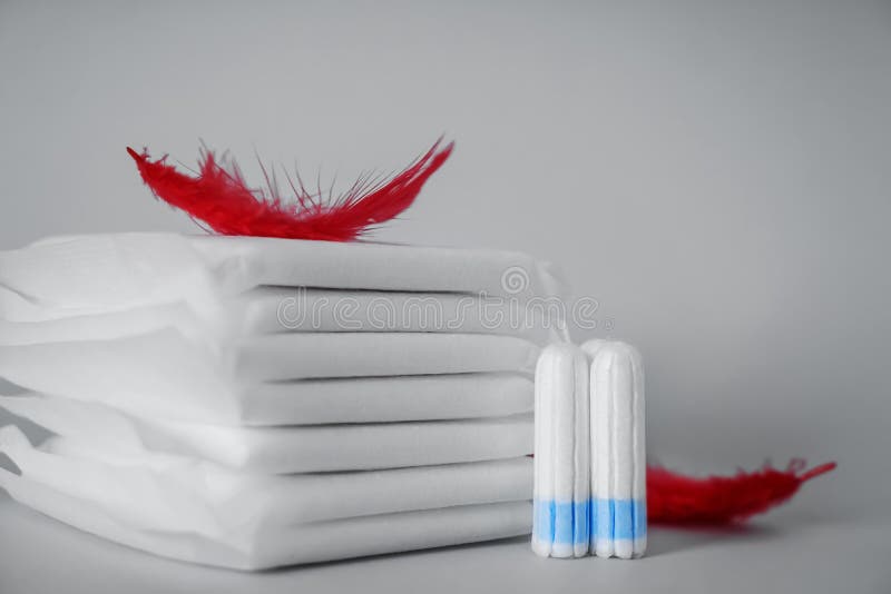 Stack of Menstrual Pads with Tampons and Red Feathers on Grey ...