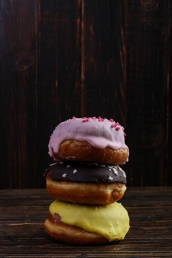 A Stack of Multi-colored Donuts with Icing and Powder on a Wooden Table ...