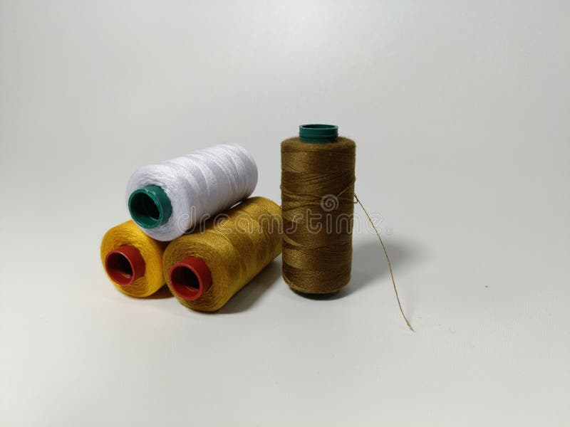 Stacked Yellow, White, and Brown Sewing Thread Spools on White ...
