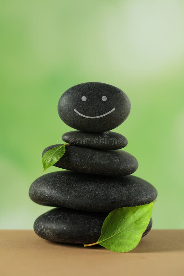Stack of Stones with Drawn Happy Face and Green Leaves on Table Against ...