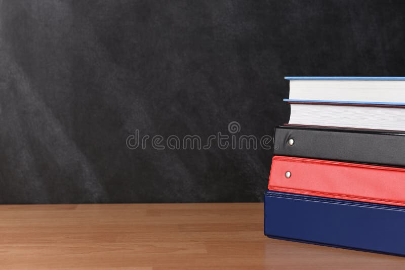 A Stack of Three Different Binders on Desk in Front of Black Board with ...