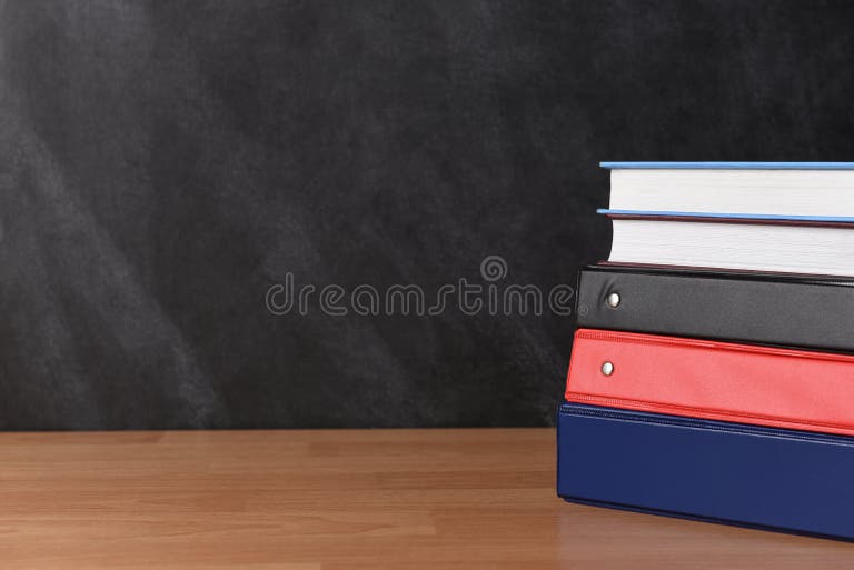 A Stack of Three Different Binders on Desk in Front of Black Board with ...