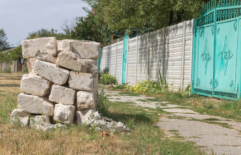A Stack of White Stone Blocks Next To the Fence, a Teal Gate in the ...