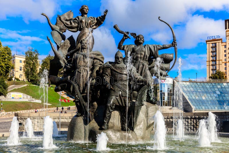 A Statue of a Group of People with a Fountain in the Background ...