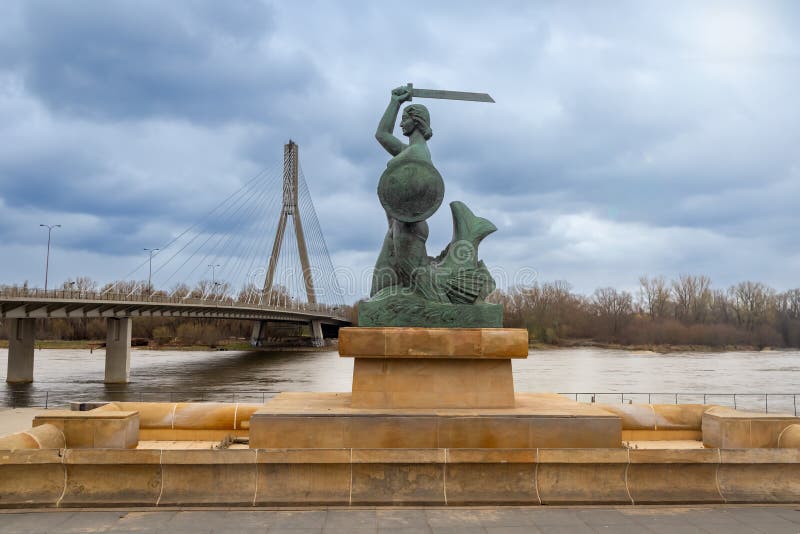 A Statue of a Mermaid with a Sword Against the Background of a Bridge ...