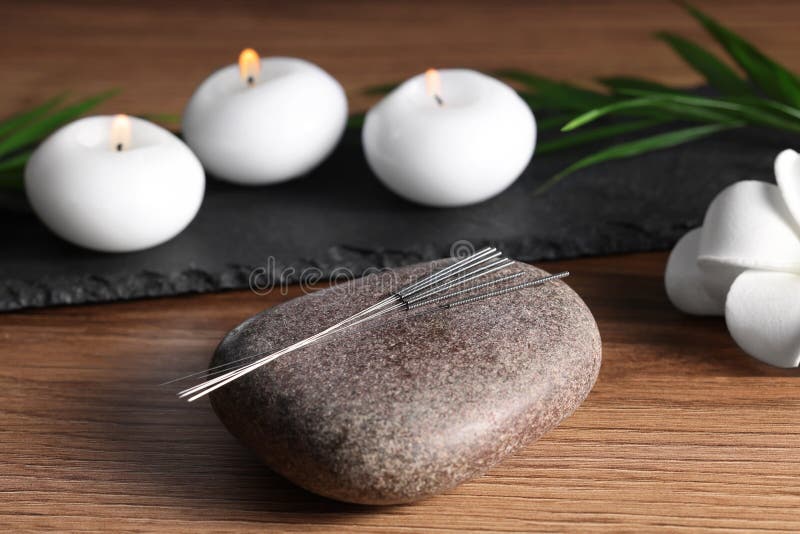 Stone with Acupuncture Needles and Burning Candles on Wooden Table ...