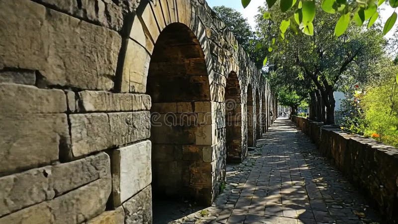 Stone Arched Colonnade Pathway with Shadows from Trees and a Low Wall ...