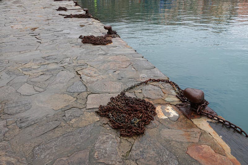 A Stone Pier Extends into Calm Blue Water, Featuring Rusty Chains and ...