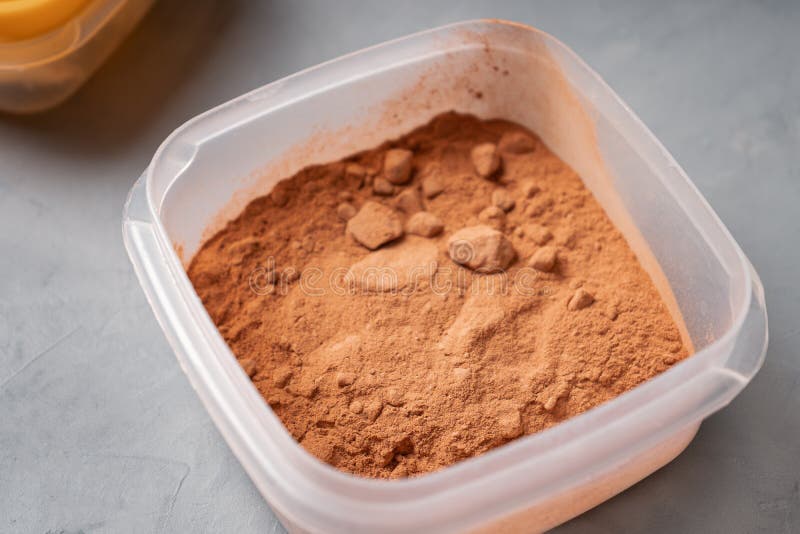 A Storage Container with Carob Powder on a Gray Concrete Surface in the ...