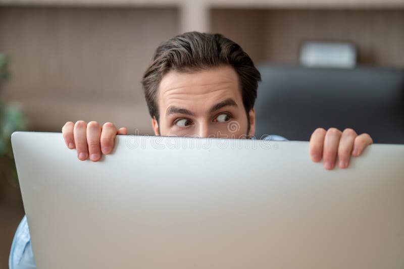 A Dark-haired Man Hiding Behind the Computer and Looking Stressed Stock ...