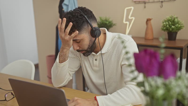 A Stressed Hispanic Man with a Beard Works on a Laptop in a Modern Home ...