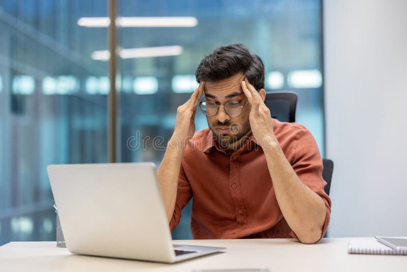 Stressed Office Worker at Desk Holding Head in Hands while Looking at ...