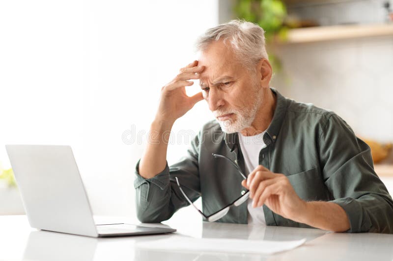 Stressed Senior Man Using Laptop while Sitting at Desk in Kitchen Stock ...