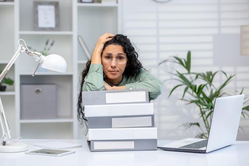 Stressed Woman Sitting at Desk with Stack of Binders in Modern Office ...