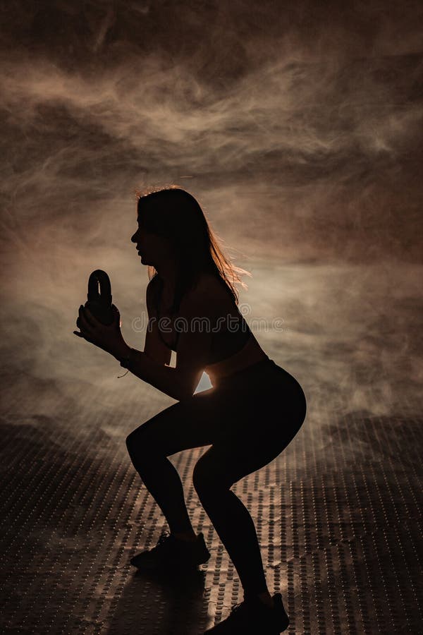 A Strong Female Athlete Performs a Deep Squat with a Kettlebell, Her ...