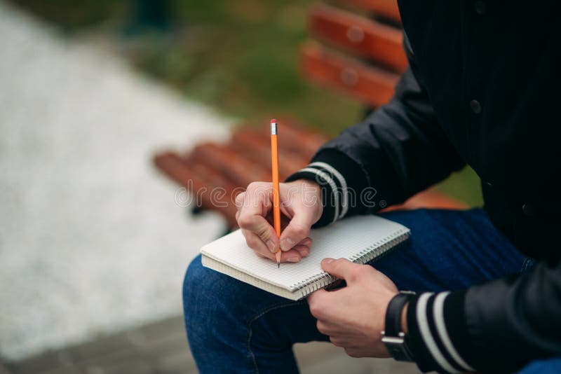 A Student in a Black Jacket Sits in a Park on a Bench Writes Down His ...