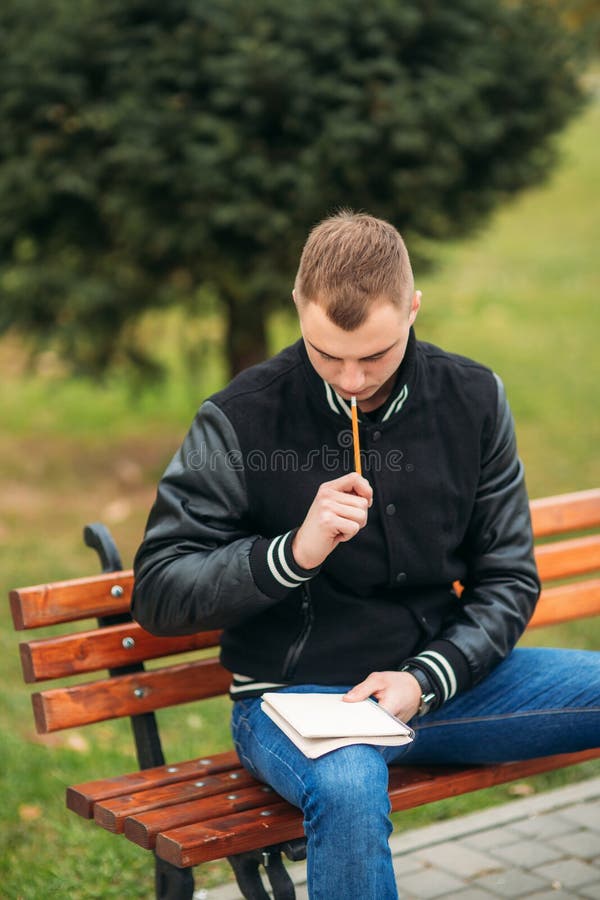 Student in a Black Jacket Sits in a Park on a Bench Writes Down His ...