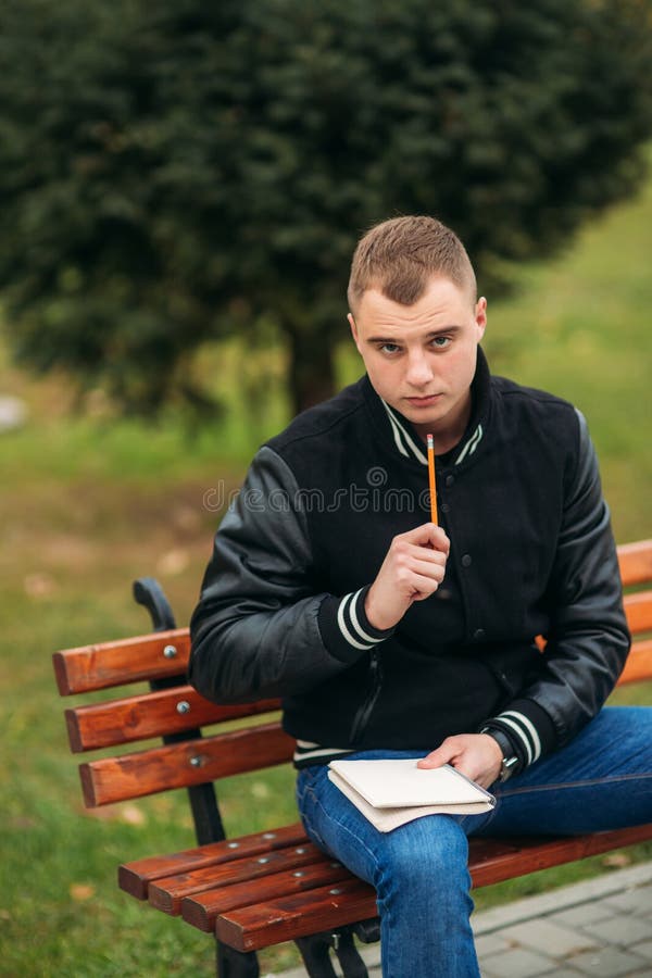 Student in a Black Jacket Sits in a Park on a Bench Writes Down His ...