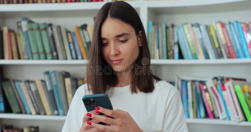 Student Girl Standing in Library and Using Smartphone, Texting Message ...