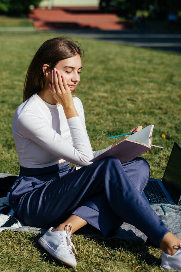 Student Girl is Studying Outside at the Summer Holliday at the University on the Green Grass ...