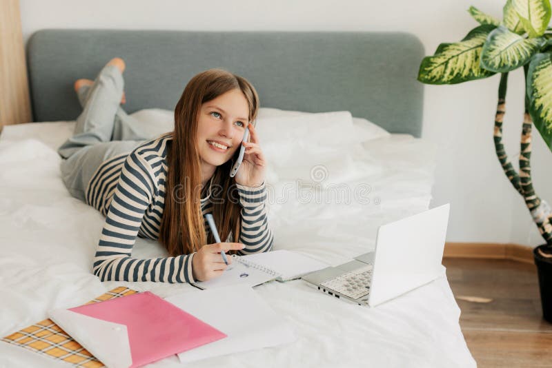 A Charming Teenage Girl is Lying on the Bed, Doing Homework with a ...