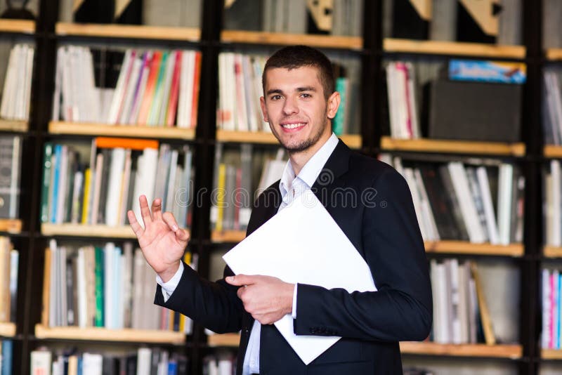 Student in Library. Handsome Young Man Holding Books and Smiling while ...